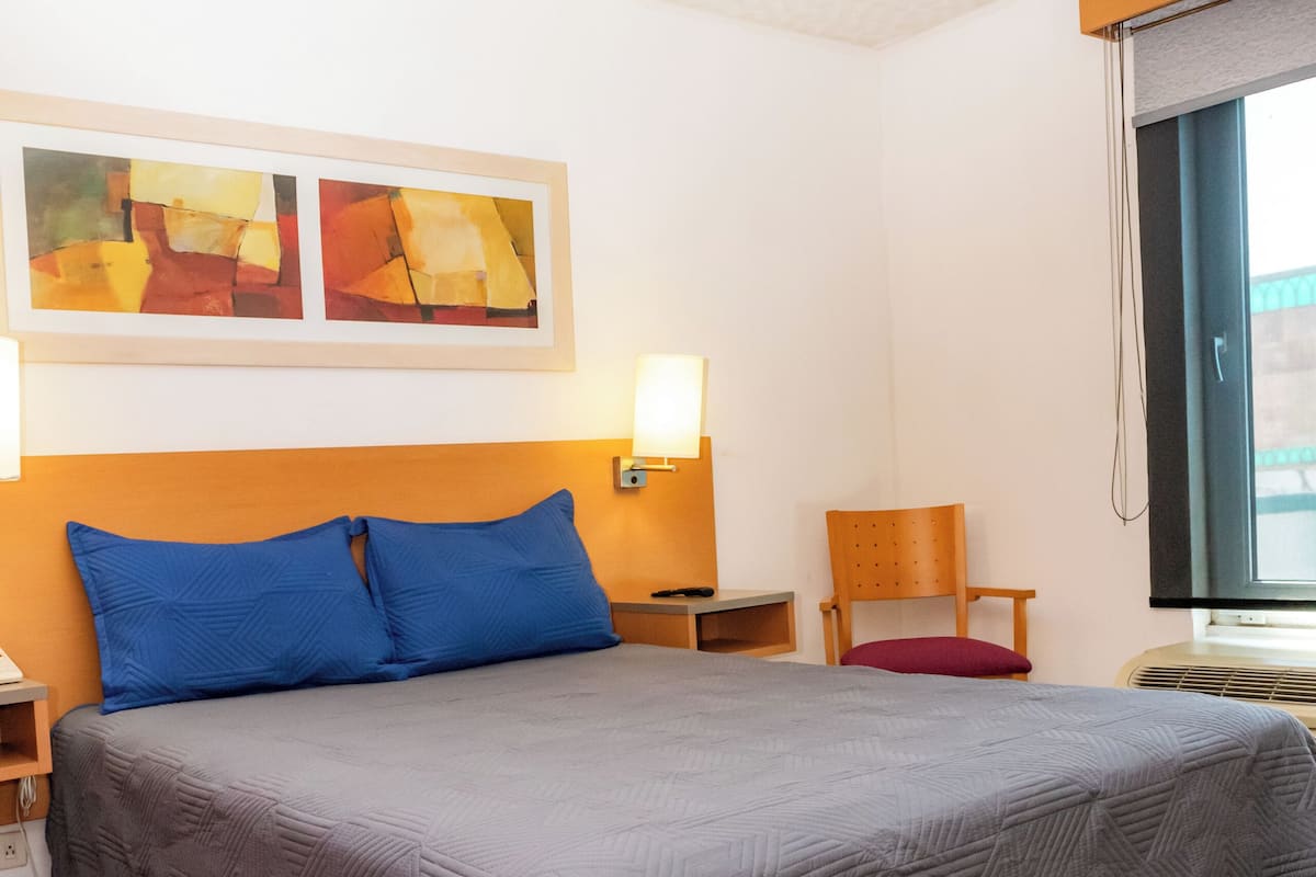 Quarto de hotel com uma cama, uma cadeira, um abajur e uma janela.