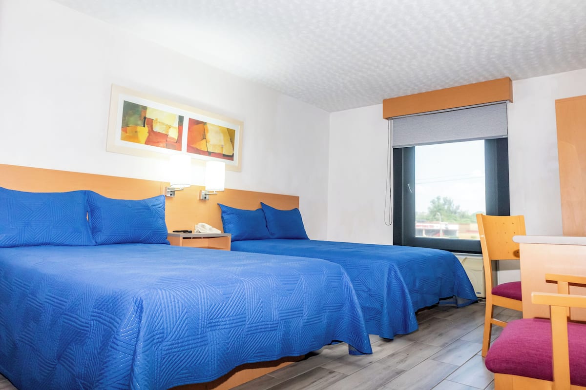 Quarto de hotel com duas camas, uma escrivaninha e uma cadeira.