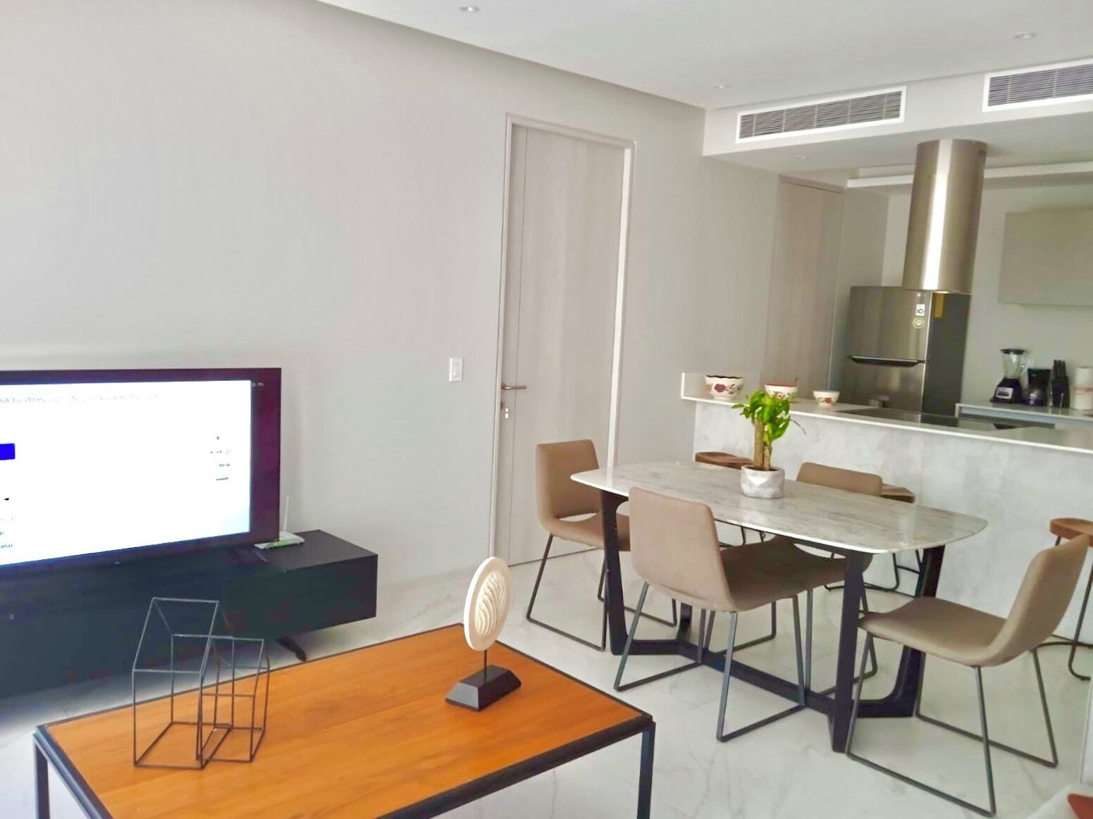 Uma sala de estar moderna com televisão de tela plana, mesa de centro de madeira e um espaço de jantar com mesa e cadeiras de mármore.