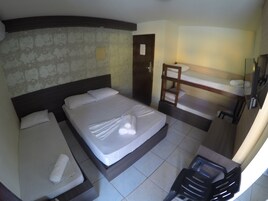 Quarto de hotel com uma cama grande, uma cama menor, uma escrivaninha, um espelho e um banheiro.