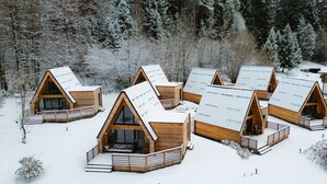 Um conjunto de cabanas de madeira com telhados inclinados, rodeadas por árvores cobertas de neve.