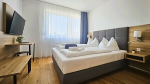 Quarto de hotel moderno com cama grande, escrivaninha, televisão e janela com cortinas.