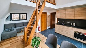 Um apartamento moderno estilo loft com escada de madeira, cozinha com armários de madeira, sofá cinza e área de jantar com mesa e cadeiras.