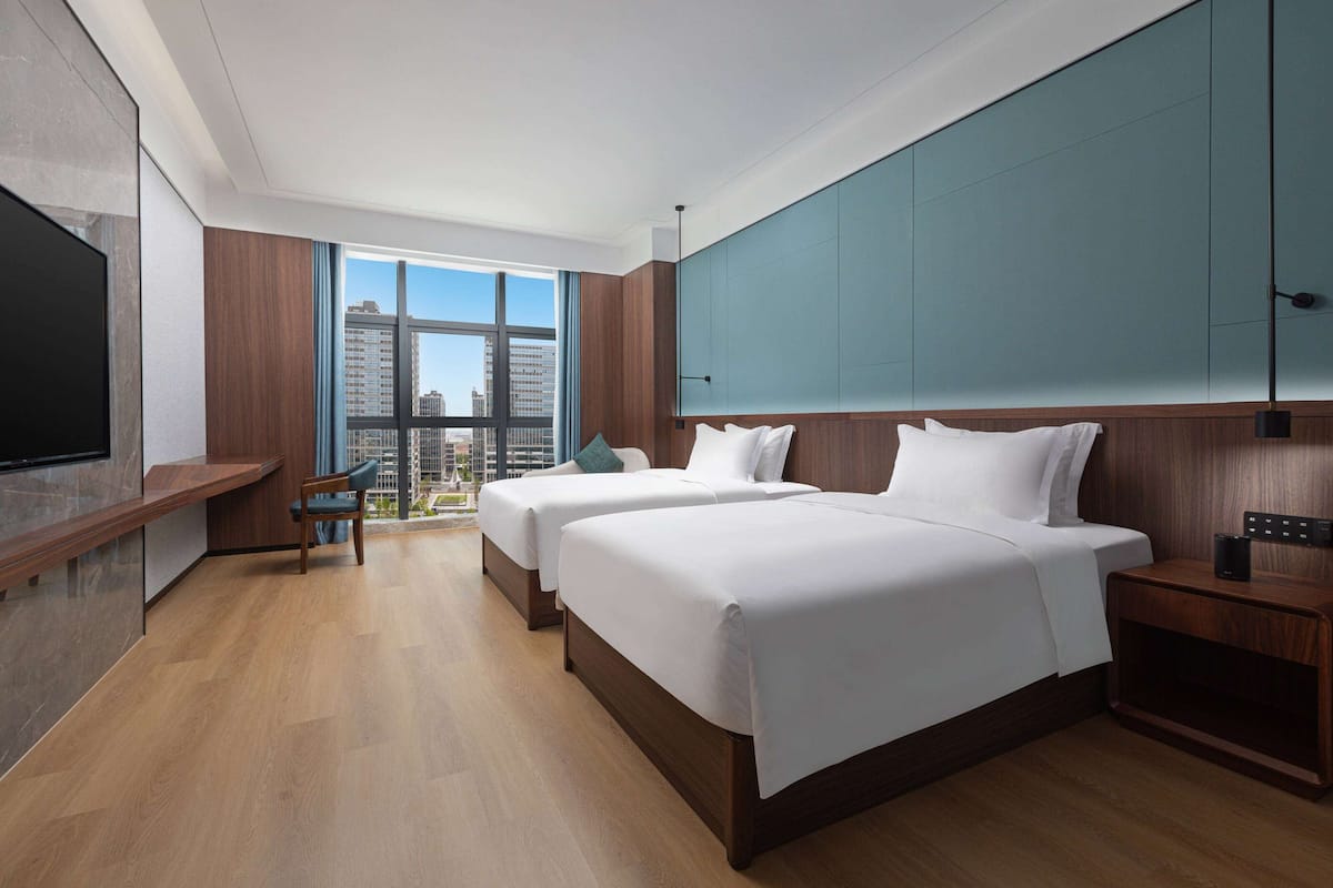 Quarto de hotel com duas camas, televisão, escrivaninha e vista para a cidade.
