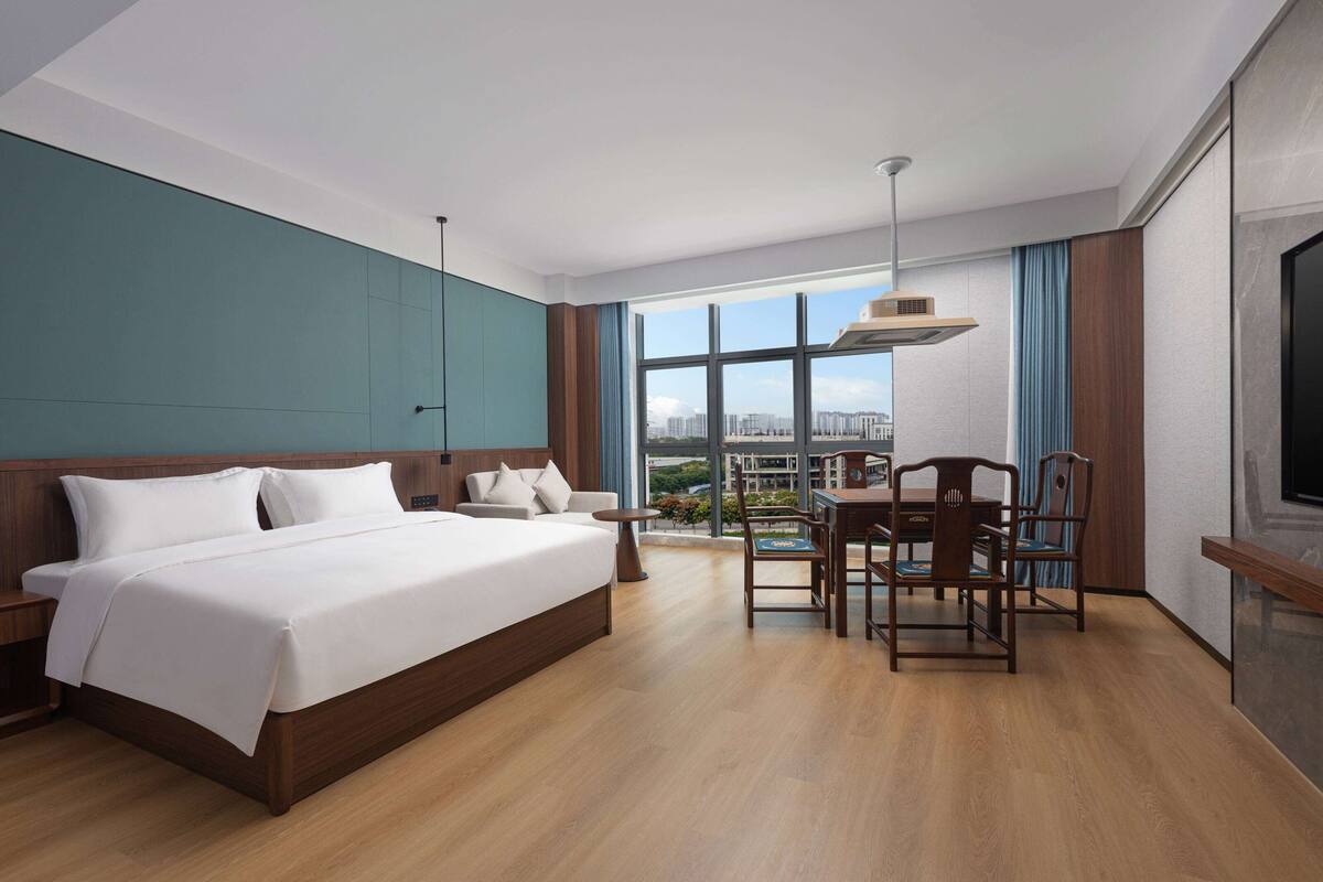 Quarto de hotel moderno com uma cama grande, área de refeições e vista para a cidade.