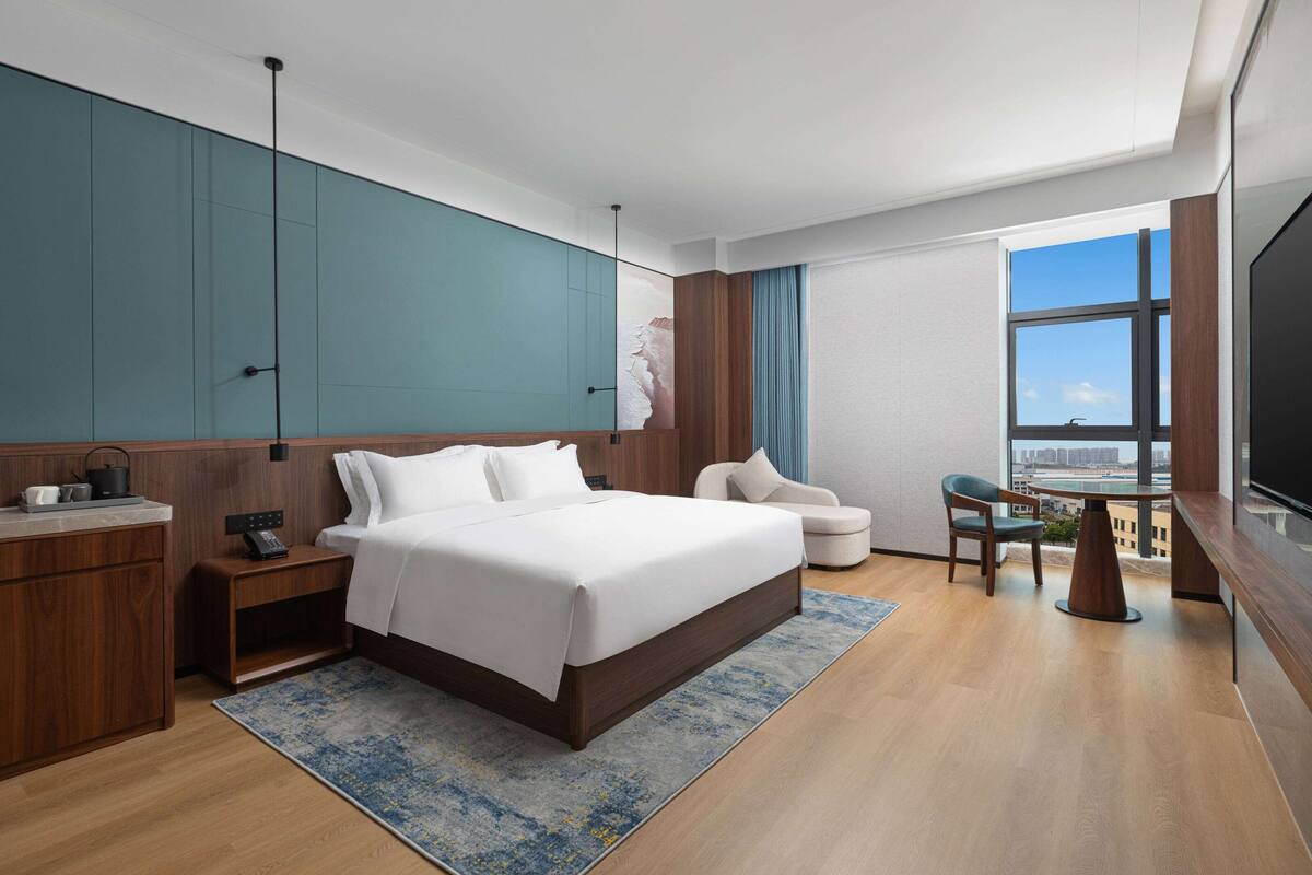 Quarto de hotel moderno com uma cama grande, uma escrivaninha, uma cadeira e uma televisão.