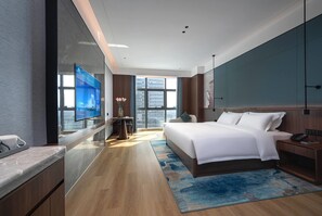 Quarto de hotel moderno com uma cama grande, escrivaninha, televisão e vista para a cidade.