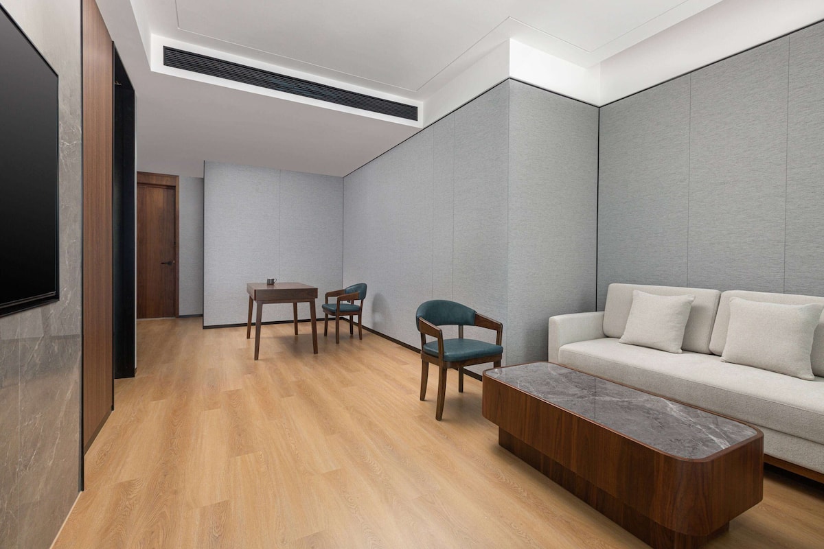 Uma sala de estar moderna, com piso de madeira, um sofá, uma mesa de centro e duas cadeiras.