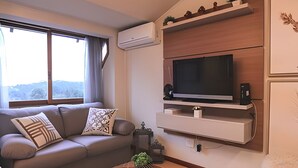 Uma sala de estar moderna com um sofá, uma TV de tela plana e uma estante com objetos decorativos.