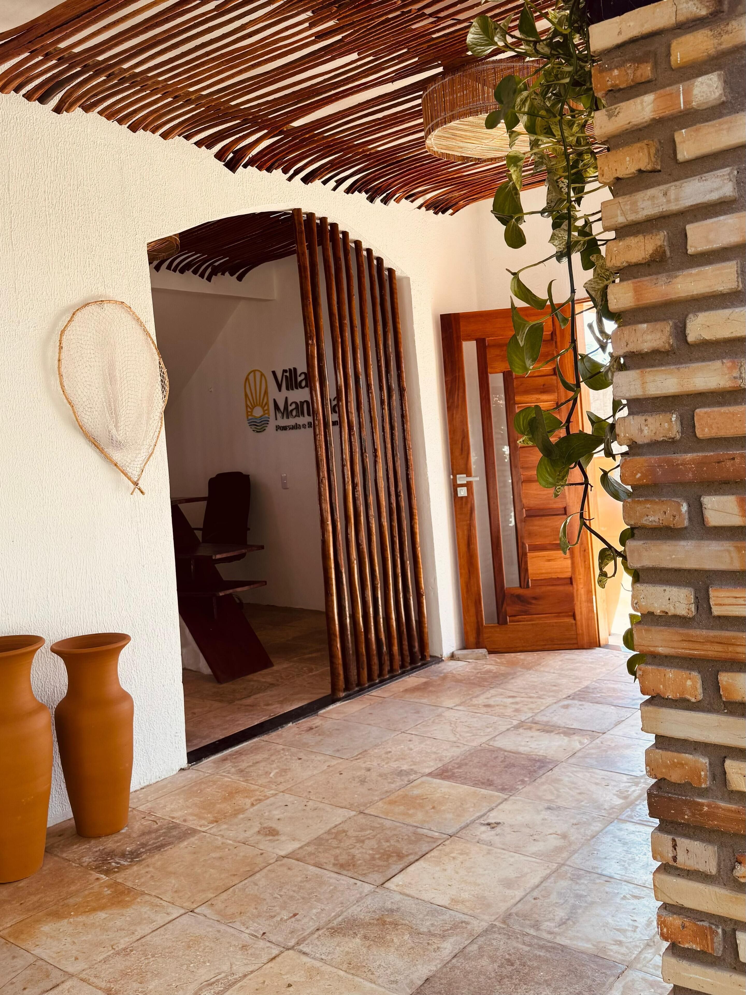 Uma área externa coberta com piso de azulejos, uma porta de madeira e uma parede com a placa 'Villa Mansa'.