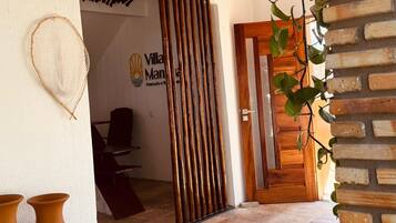 Uma área externa coberta com piso de azulejos, uma porta de madeira e uma parede com a placa 'Villa Mansa'.