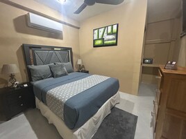 Quarto com cama, mesas de cabeceira, ar-condicionado fixado na parede, ventilador de teto, pintura e armário de madeira.