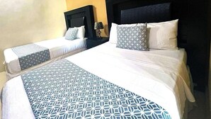 Quarto de hotel com duas camas, uma cama de casal com colcha estampada em padrão geométrico e duas camas menores com colchas estampadas.
