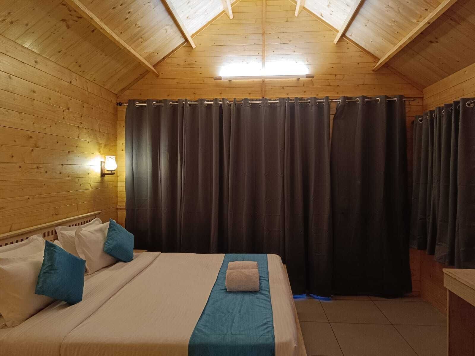 Um quarto acolhedor com teto de madeira, uma cama com roupa de cama azul e uma cortina.