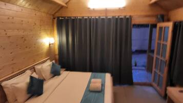 Quarto de cabana de madeira com cama, almofadas, televisão e cortina.