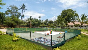 Área de lazer ao ar livre cercada, com piso de rede, rodeada por vegetação exuberante e palmeiras.