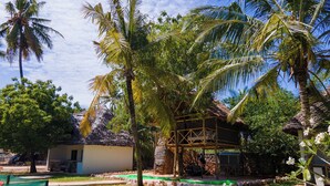 Um resort tropical com estrutura de telhado de palha, palmeiras e um gramado bem cuidado.