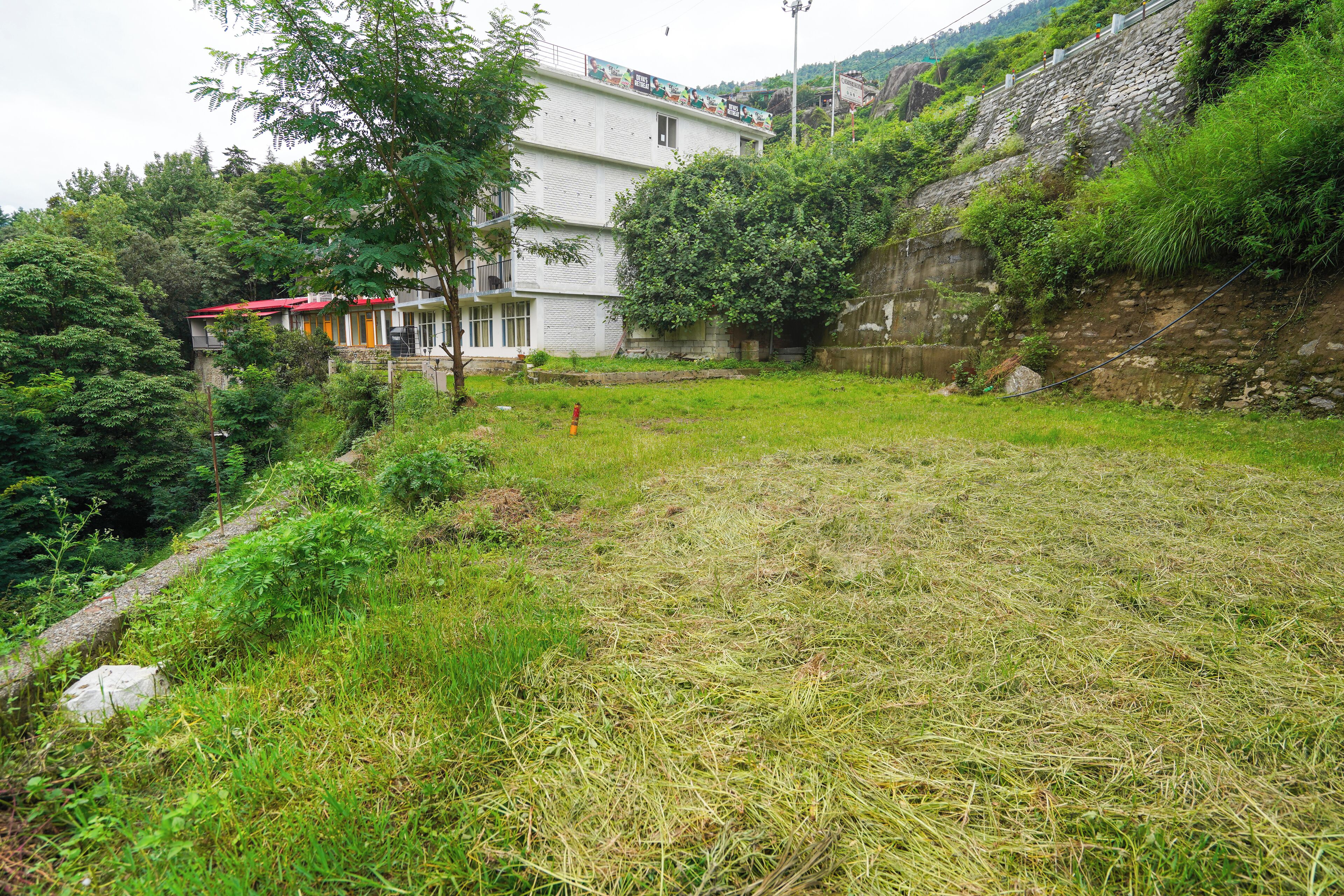 Um edifício com telhado vermelho, rodeado por vegetação e uma parede de pedra.