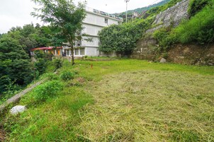 Um edifício com telhado vermelho, rodeado por vegetação e uma parede de pedra.