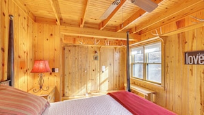 Quarto de cabana de madeira com cama, mesa de cabeceira, abajur, janela e porta.