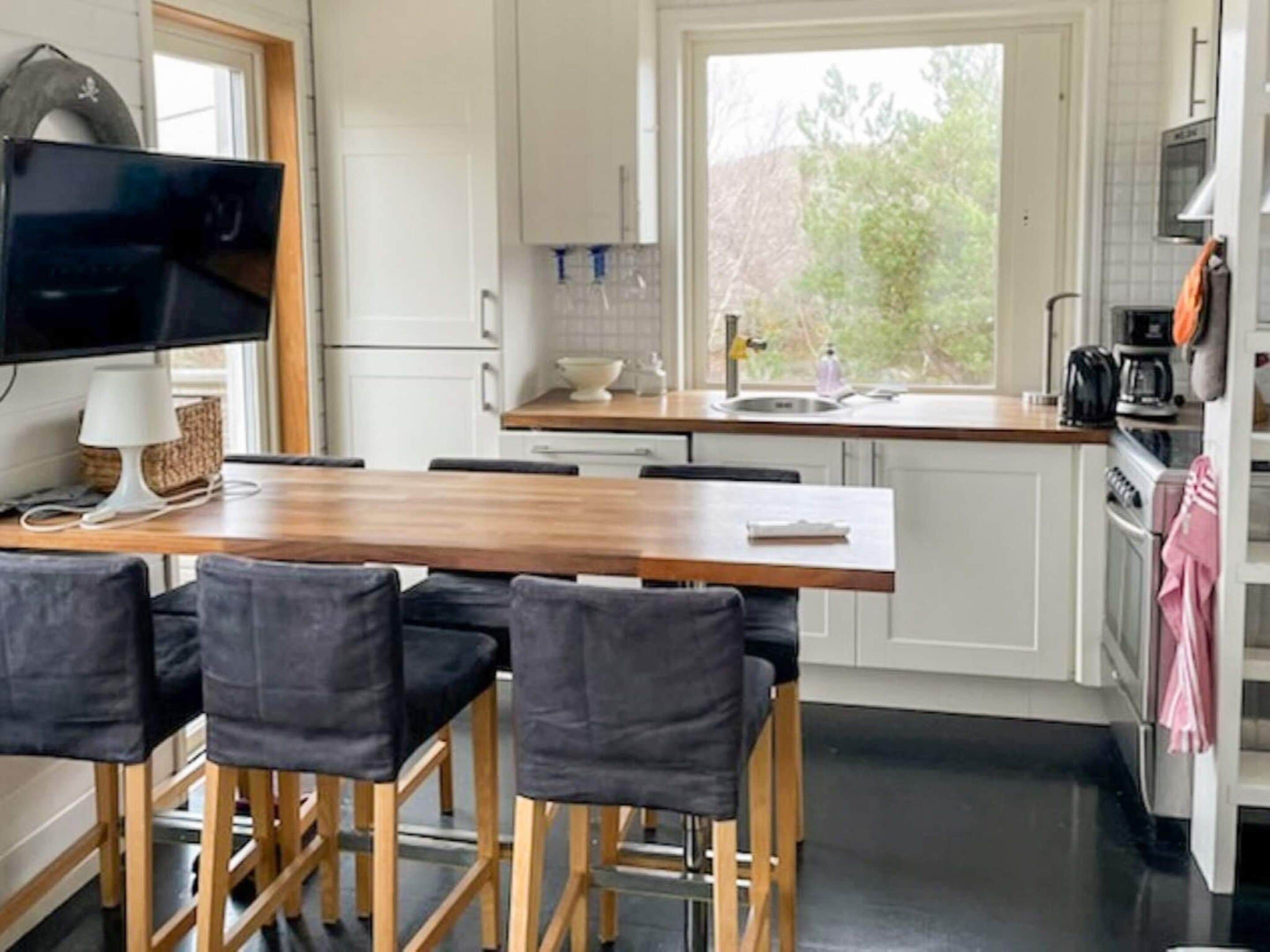 Cozinha moderna com mesa e cadeiras de madeira, forno embutido e janela com vista para o exterior.
