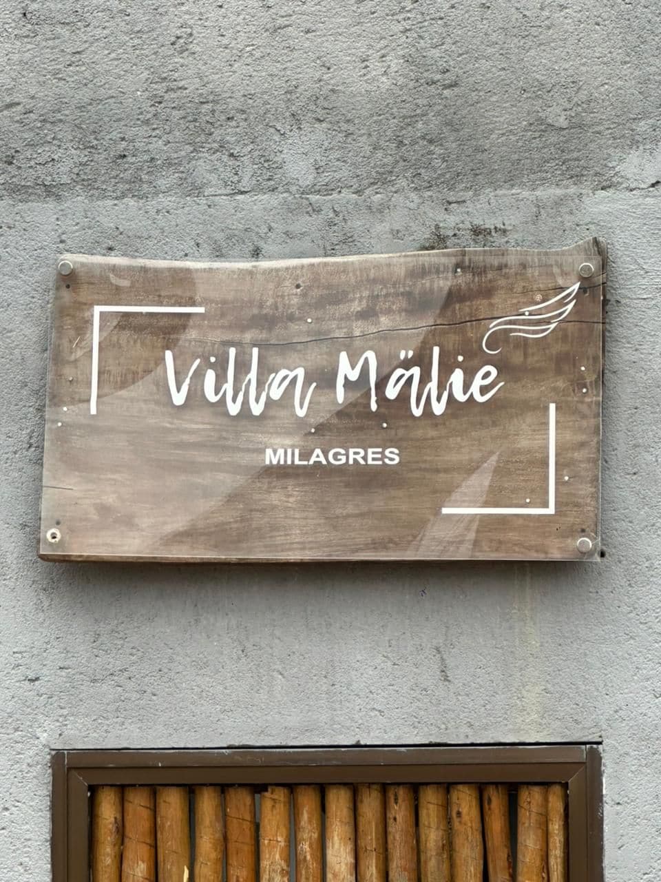 Uma placa de madeira com o texto 'Villa Mähle MILAGRES' fixada numa parede.
