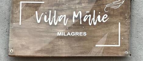 Uma placa de madeira com o texto 'Villa Mähle MILAGRES' fixada numa parede.