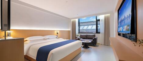 Quarto de hotel moderno com uma cama grande, um sofá, uma TV e vista para a cidade pela janela.