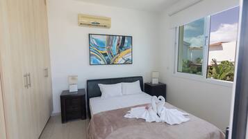 Um quarto com cama, mesa de cabeceira, guarda-roupa, pintura e janela com vista.