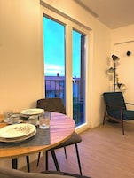 Uma sala de jantar com uma mesa redonda, cadeiras e vista para uma varanda através de grandes janelas.
