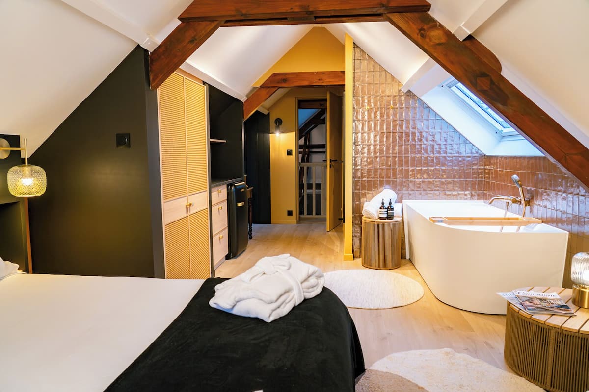Quarto com uma cama grande, banheiro com banheira e claraboia.