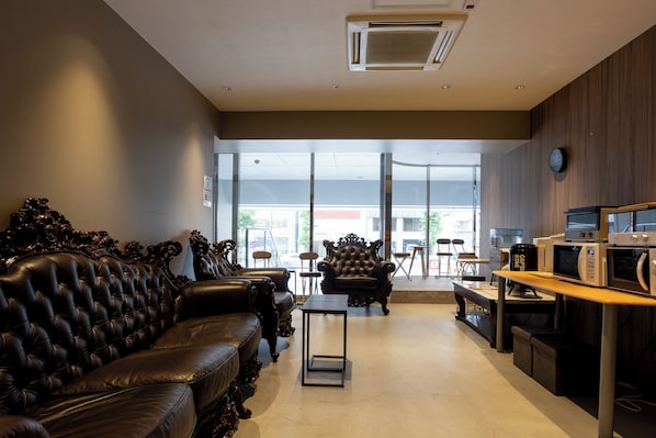 Um interior moderno com um sofá de couro, uma poltrona clássica, uma mesa pequena e um micro-ondas.