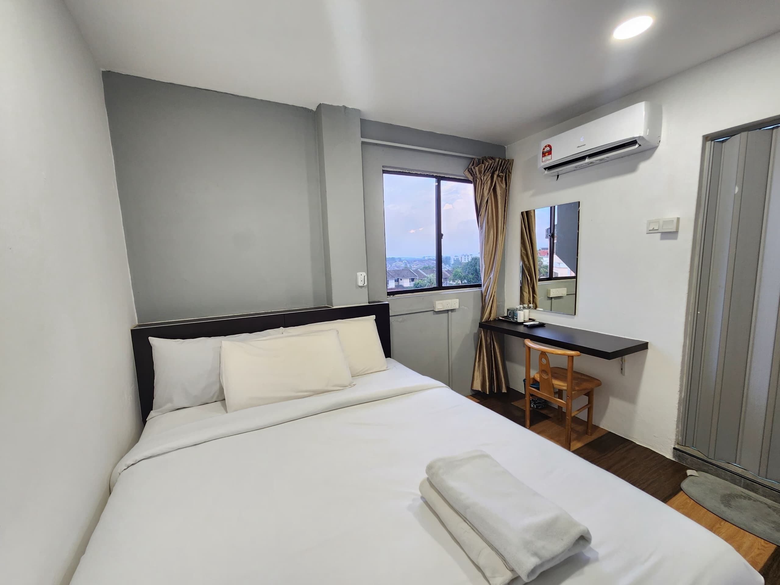 Quarto de hotel com uma cama, escrivaninha, cadeira, janela e ar condicionado.