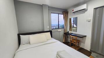 Quarto de hotel com uma cama, escrivaninha, cadeira, janela e ar condicionado.