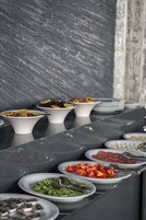 Buffet com diversos pratos, incluindo saladas, frutas e carnes.