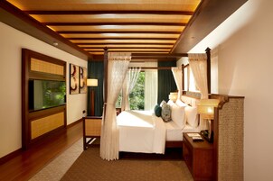 Quarto de hotel com cama, mesa de cabeceira, abajur e vista para o verde pela janela.