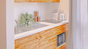 Cozinha compacta com armários de madeira, pia, cafeteira e lixeira.
