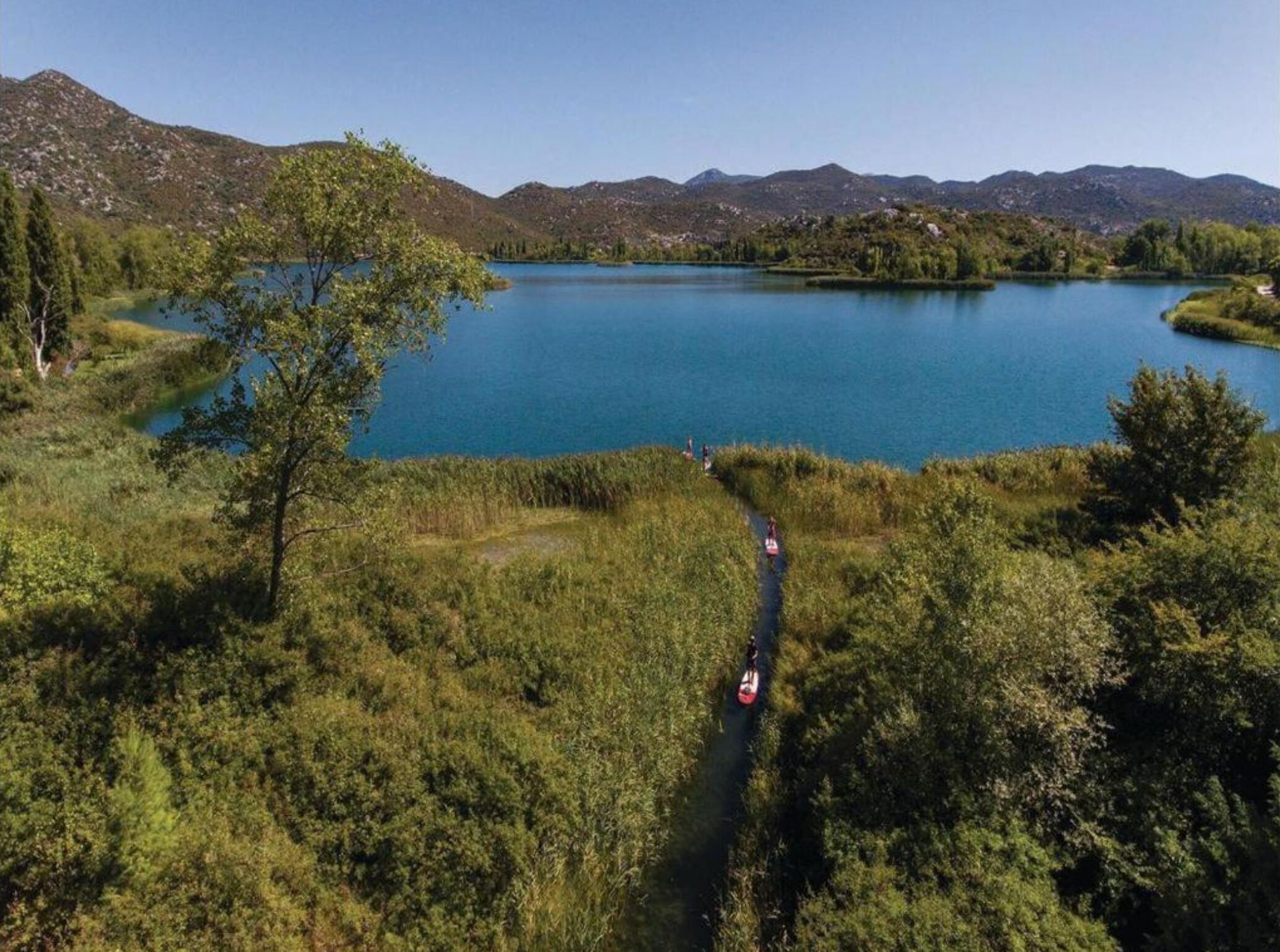 Um lago rodeado por colinas, com uma trilha estreita que leva a um barco.