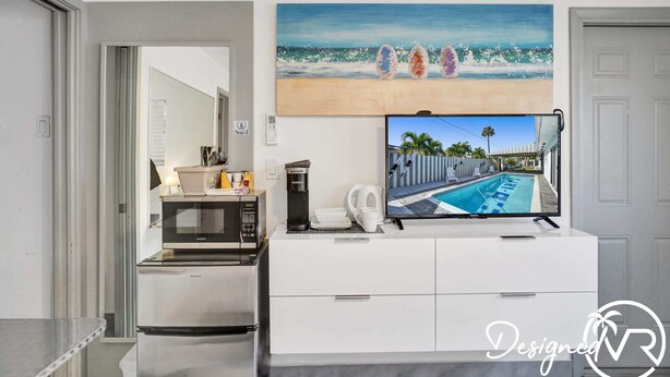 Cozinha moderna com micro-ondas, cafeteira e TV exibindo uma cena de piscina.
