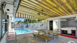 Uma área de piscina com deck de madeira, um banco e um espaço de estar coberto.