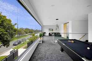 Quarto moderno com mesa de bilhar, área de jantar e vista para a estrada e vegetação.