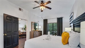Quarto de hotel com cama grande, ventoinha no teto, penteadeira, espelho e vista para o exterior.