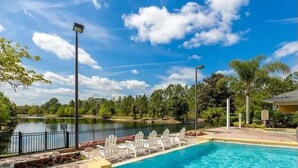 Piscina com cadeiras de descanso brancas e vista para um lago.