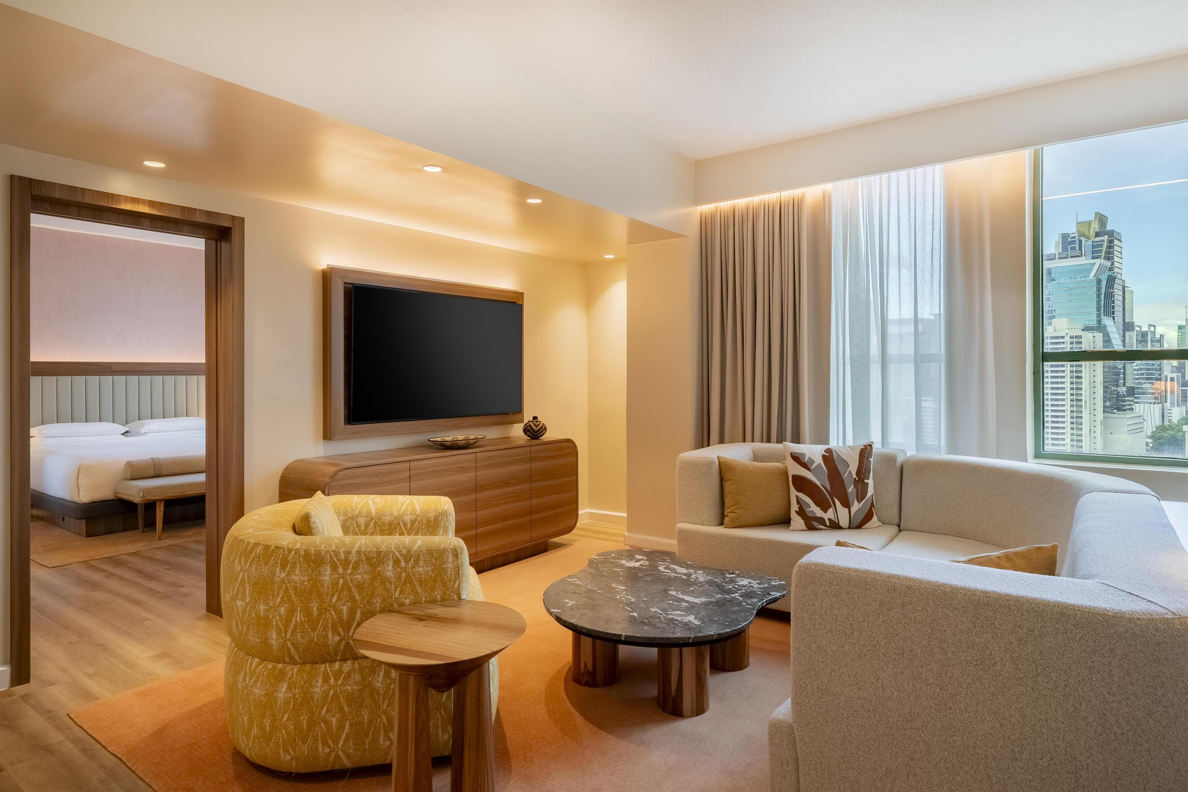 Quarto de hotel moderno com cama, sofá, televisão e vista para a cidade.