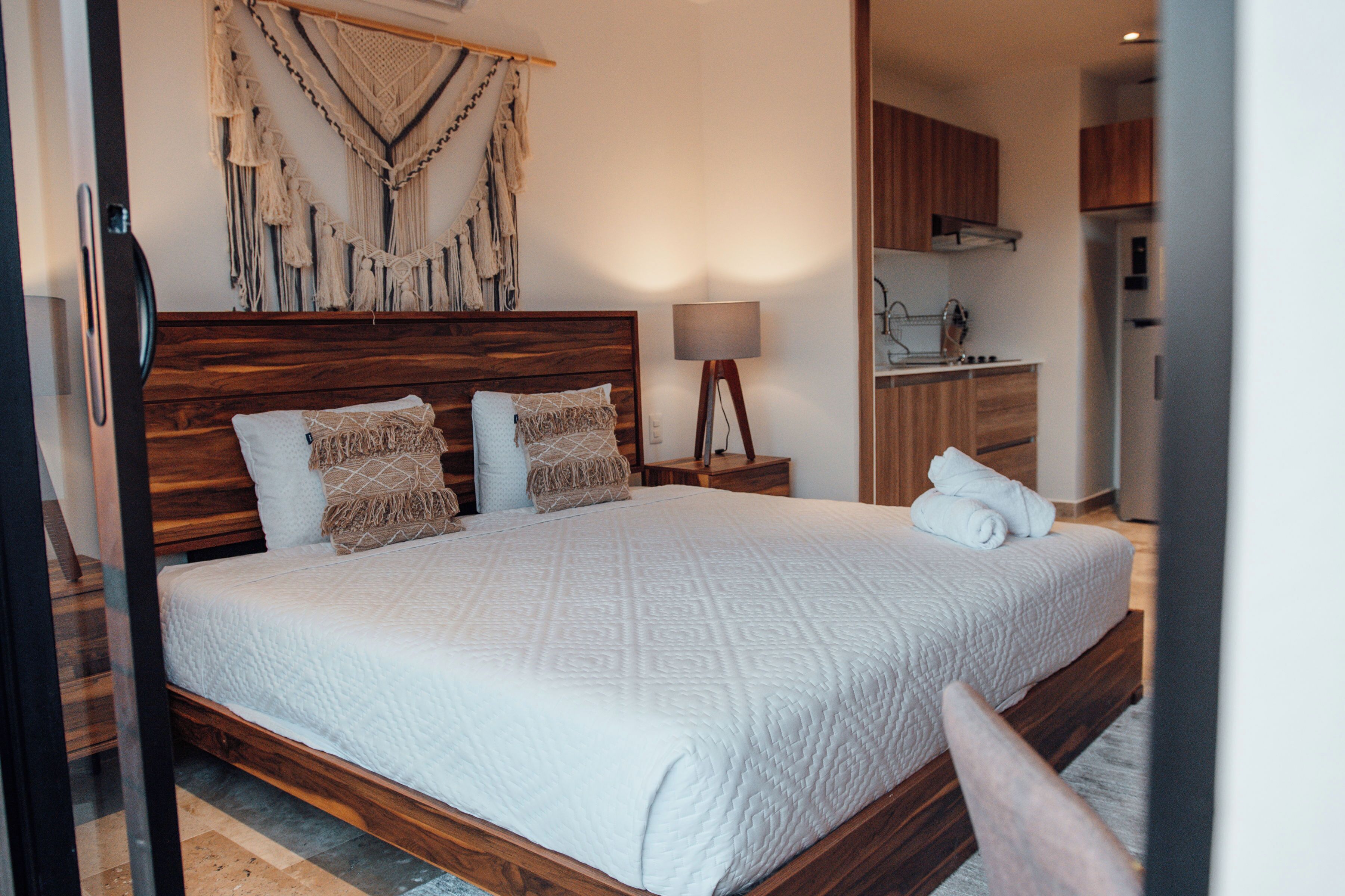Quarto com cama grande, cabeceira de madeira e um pendente de macramé na parede.