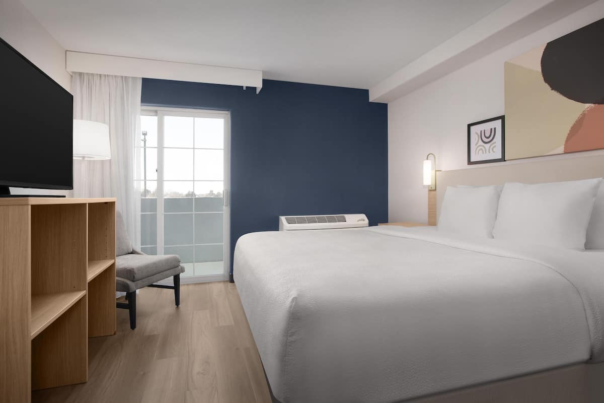 Quarto de hotel moderno com uma cama grande, televisão, escrivaninha e janela com cortinas.