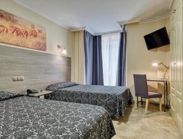 Quarto de hotel com duas camas, uma escrivaninha, uma cadeira, uma televisão e um quadro na parede.