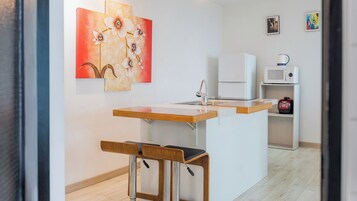 Cozinha compacta com bancada de madeira, dois bancos altos, micro-ondas e cafeteira.