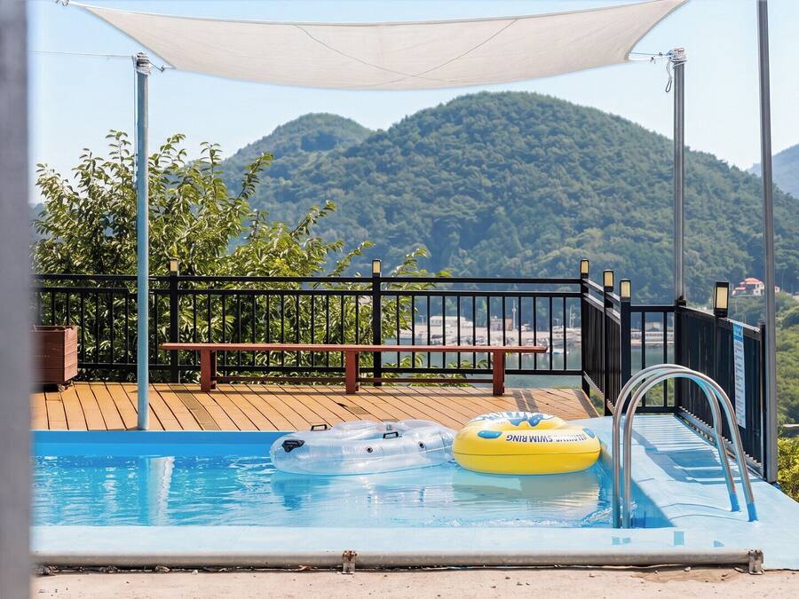Piscina com boias infláveis, deck de madeira, um banco e vista para uma paisagem montanhosa.