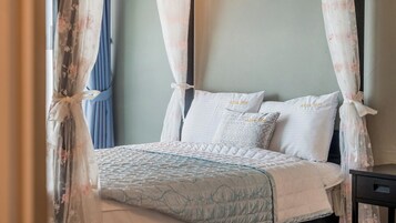 Uma cama com colcha acolchoada, dois travesseiros e dossel com motivos florais.